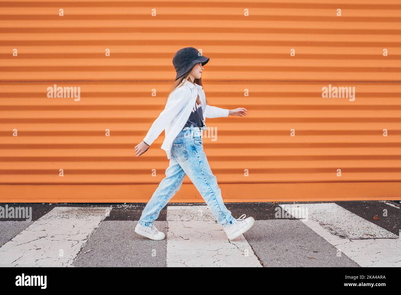 Little fashion-dressed girl funny walking crossing a pedestrian zebra ...