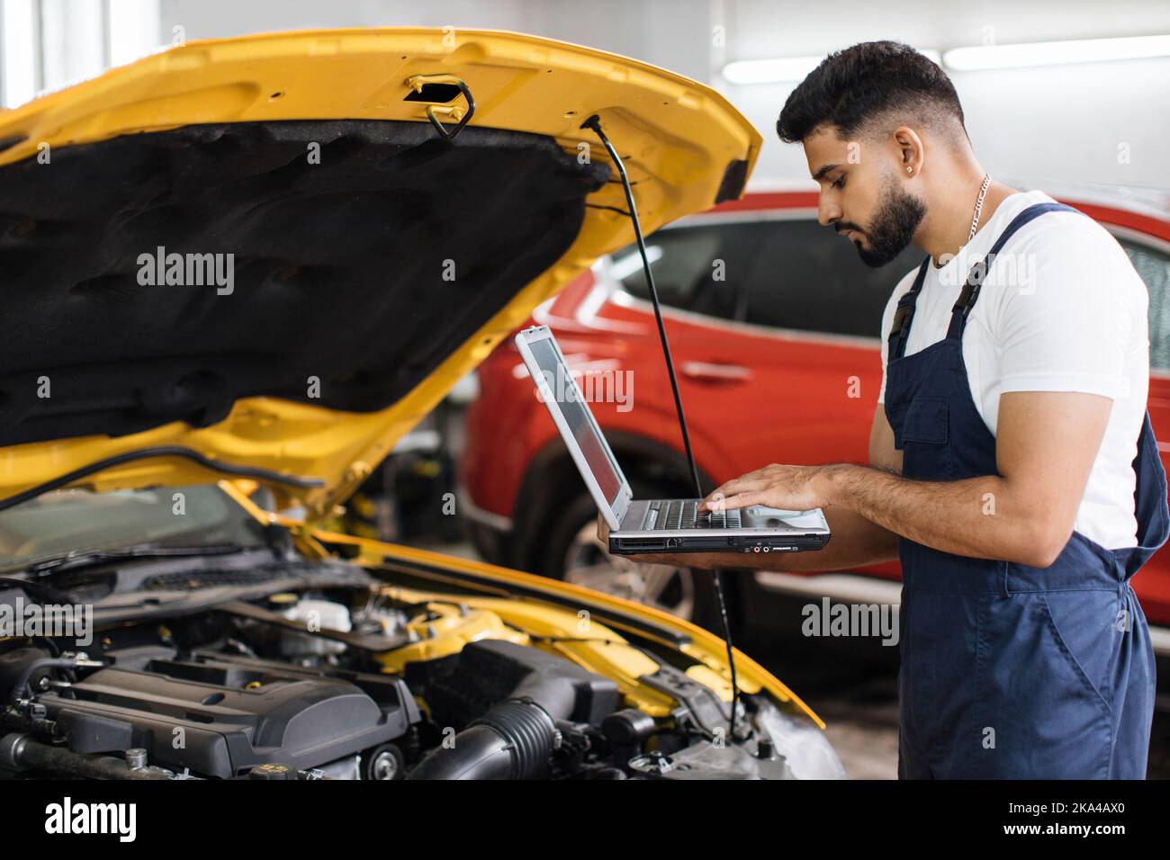 Bearded male mechanic using laptop, recording automobile engine checks ...