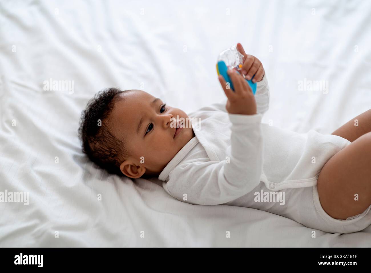Cute Black Baby Holding Rattle Toy While Lying On Bed At Home Stock ...