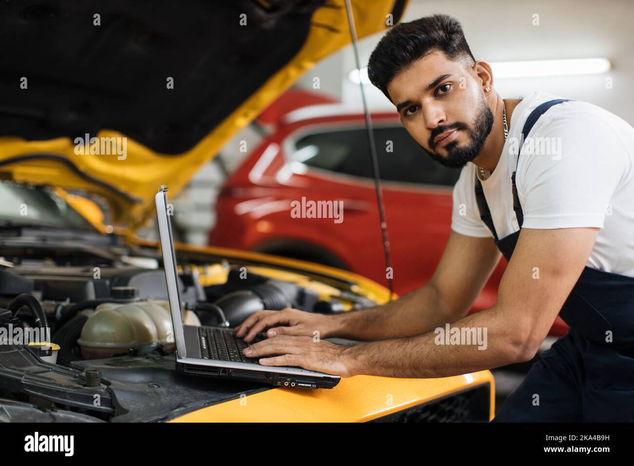 Young man car mechanic maintains vehicle using diagnostic laptop ...