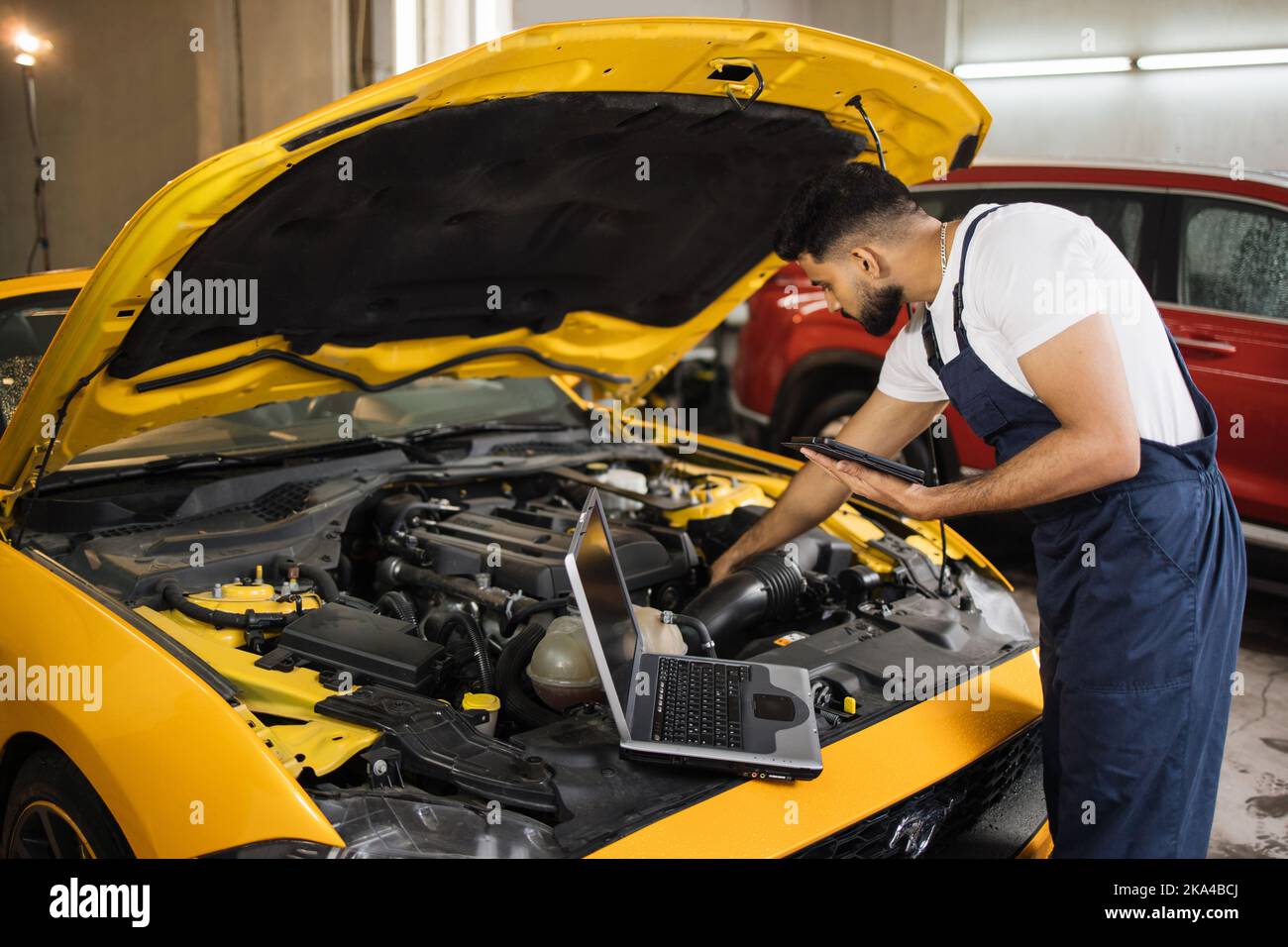 Young mechanic using tablet computer, recording automobile engine ...