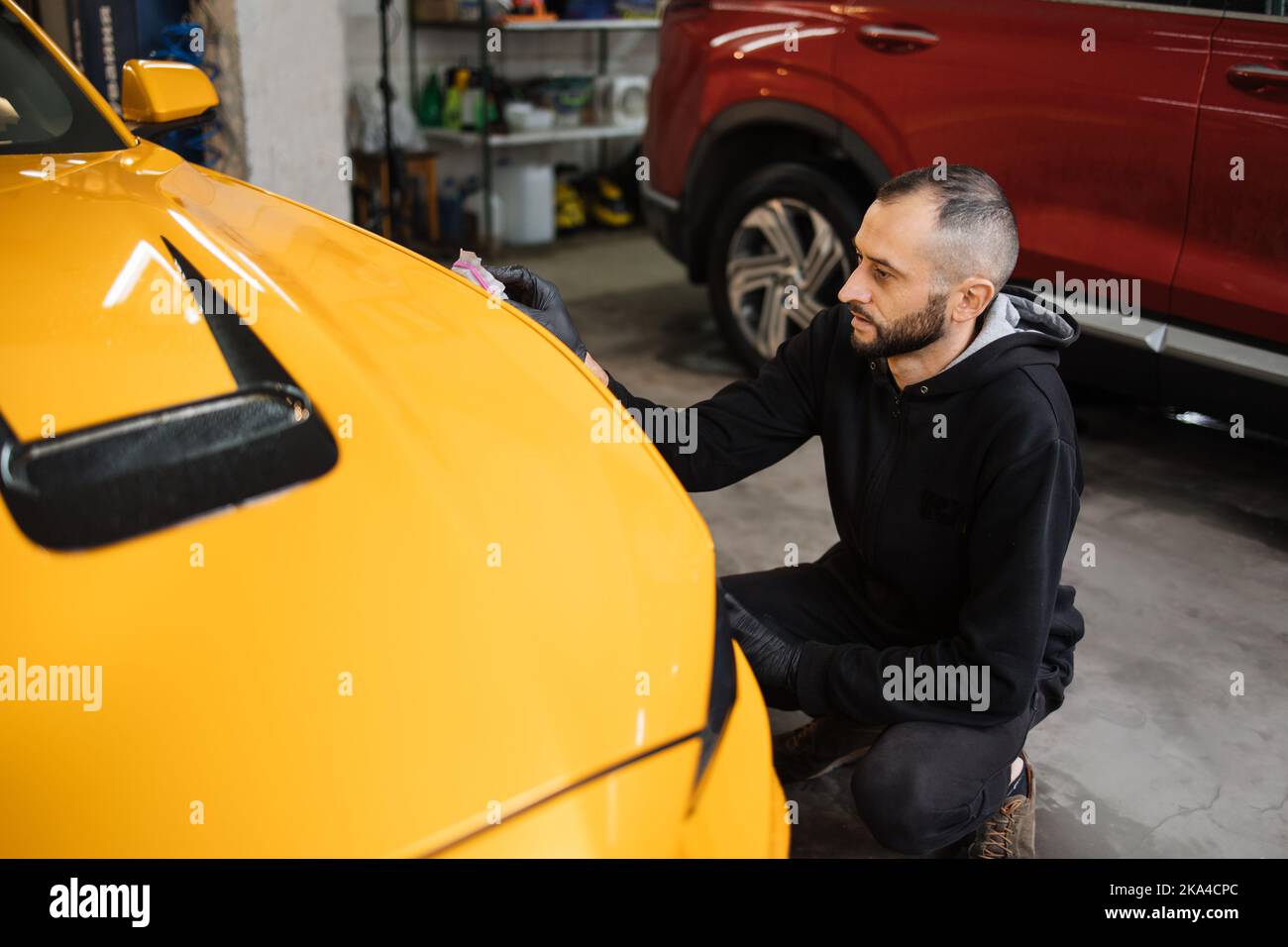 Side view of young man, car polish service worker polishing car hood ...