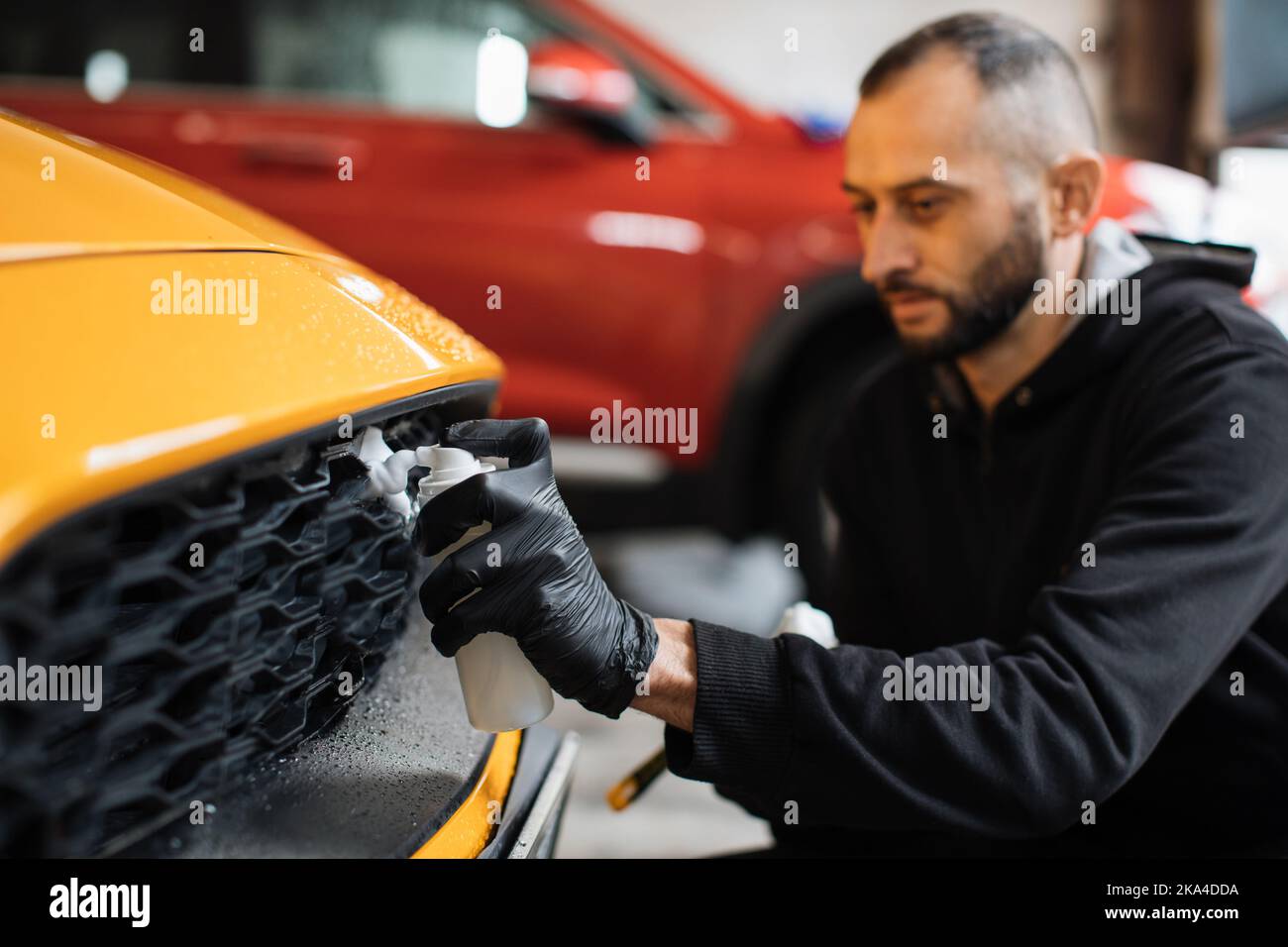 Detailing manual cleaning with soap at car wash. Young male worker in ...