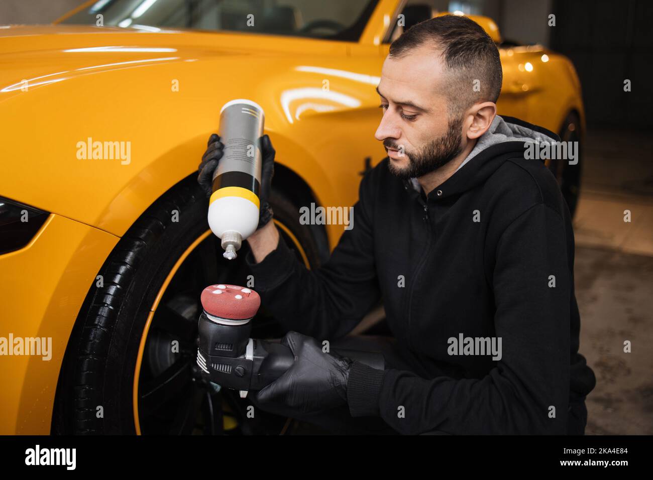 Car detailing services - polishing of yellow car. Auto service worker, wearing black clothes ...