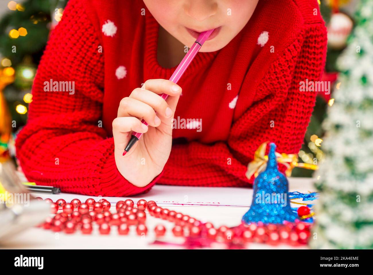 Cute boy in Santa hat writes a letter to Santa near the Christmas tree ...