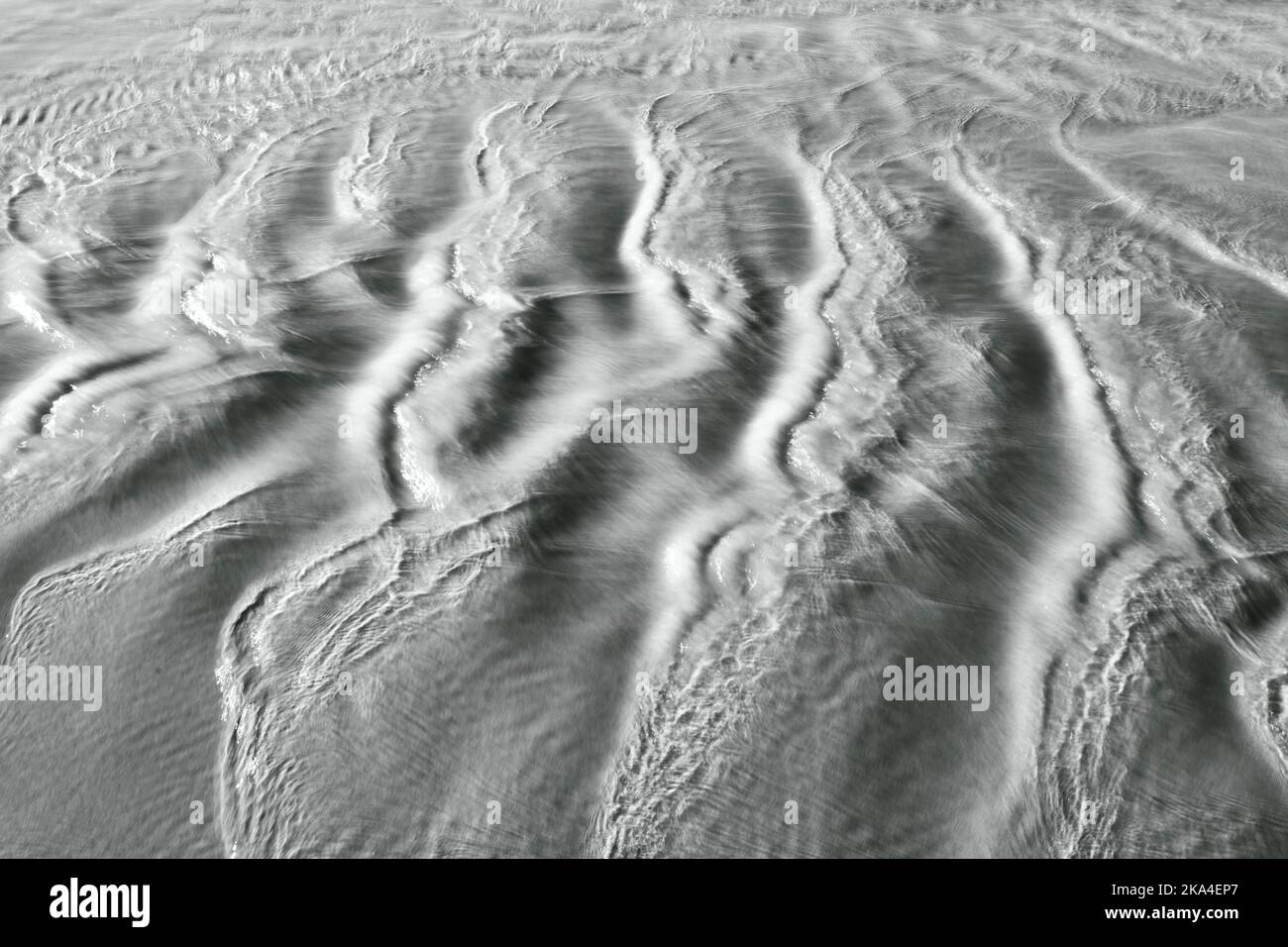 Ocean waves moving the sand with its current; creating abstract lines ...