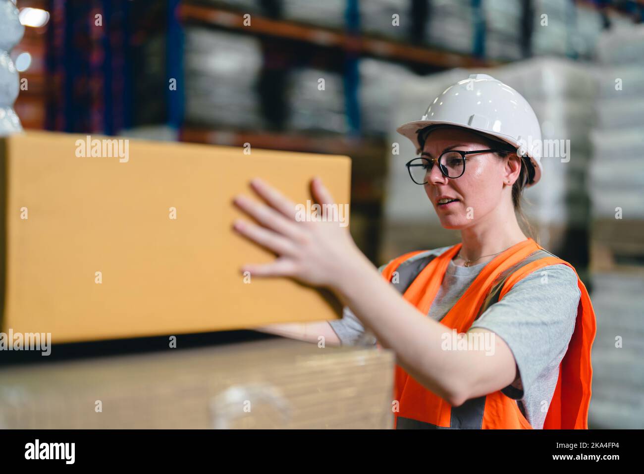 A Caucasian warehouse worker stacking the box on the pallet in a large ...