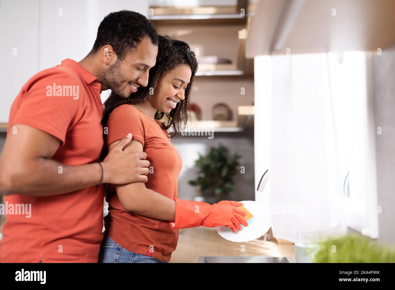 Cheerful young black male hugs wife in rubber gloves, lady washes ...