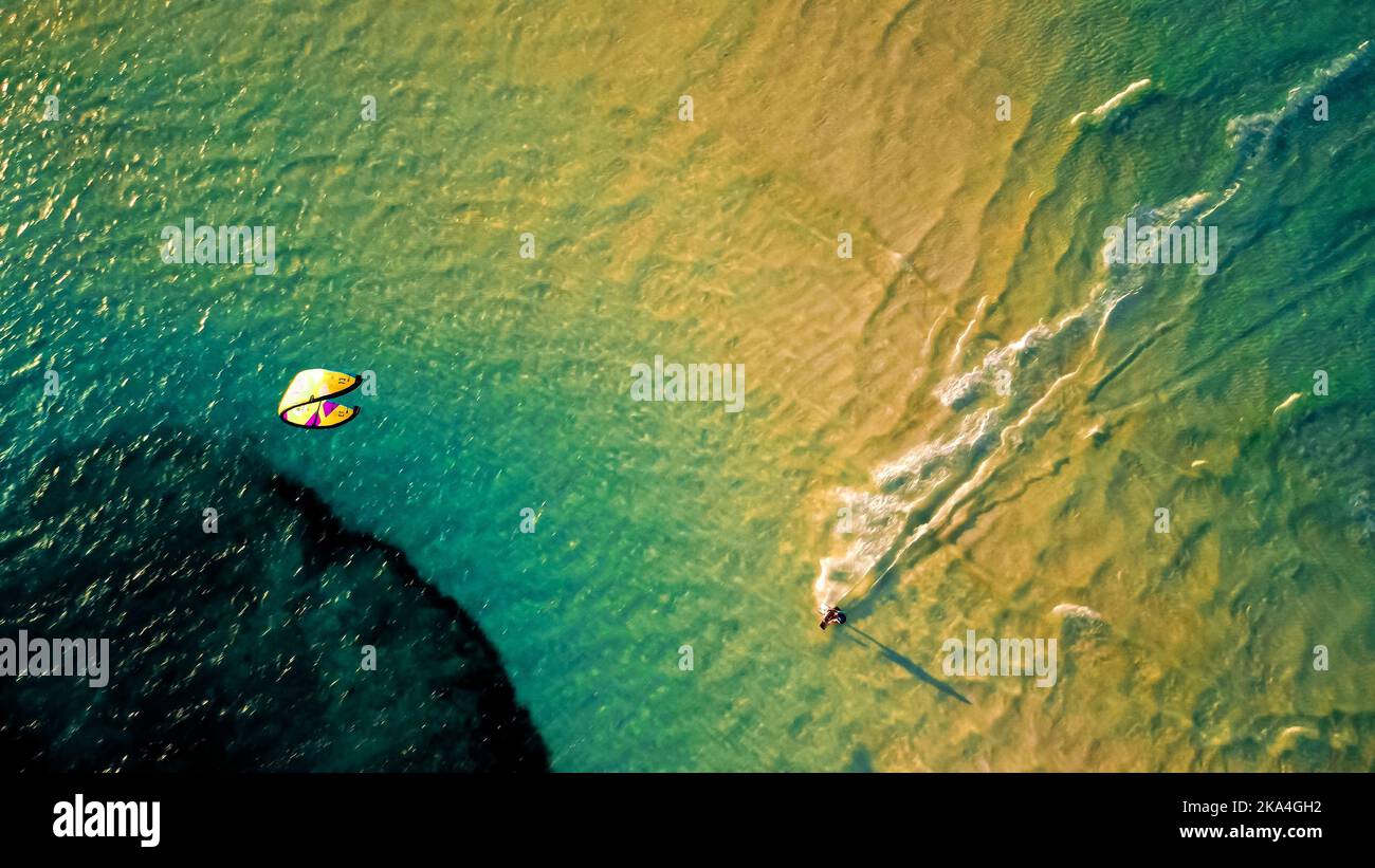 An aerial drone shot of a kite surfer surfing on the calm waters of the ...