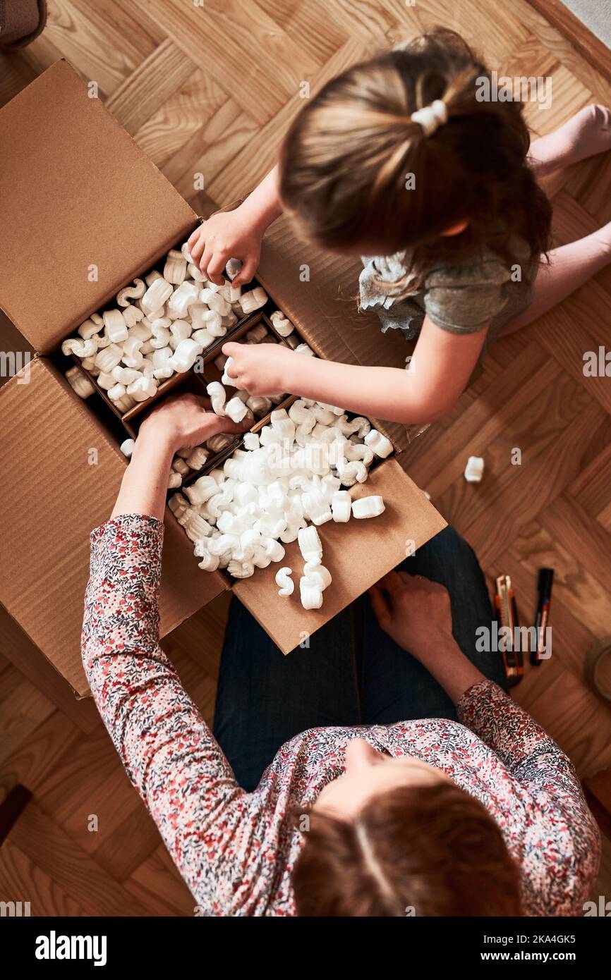 Woman unpacking a cardboard box parcel in room at home. Little girl ...