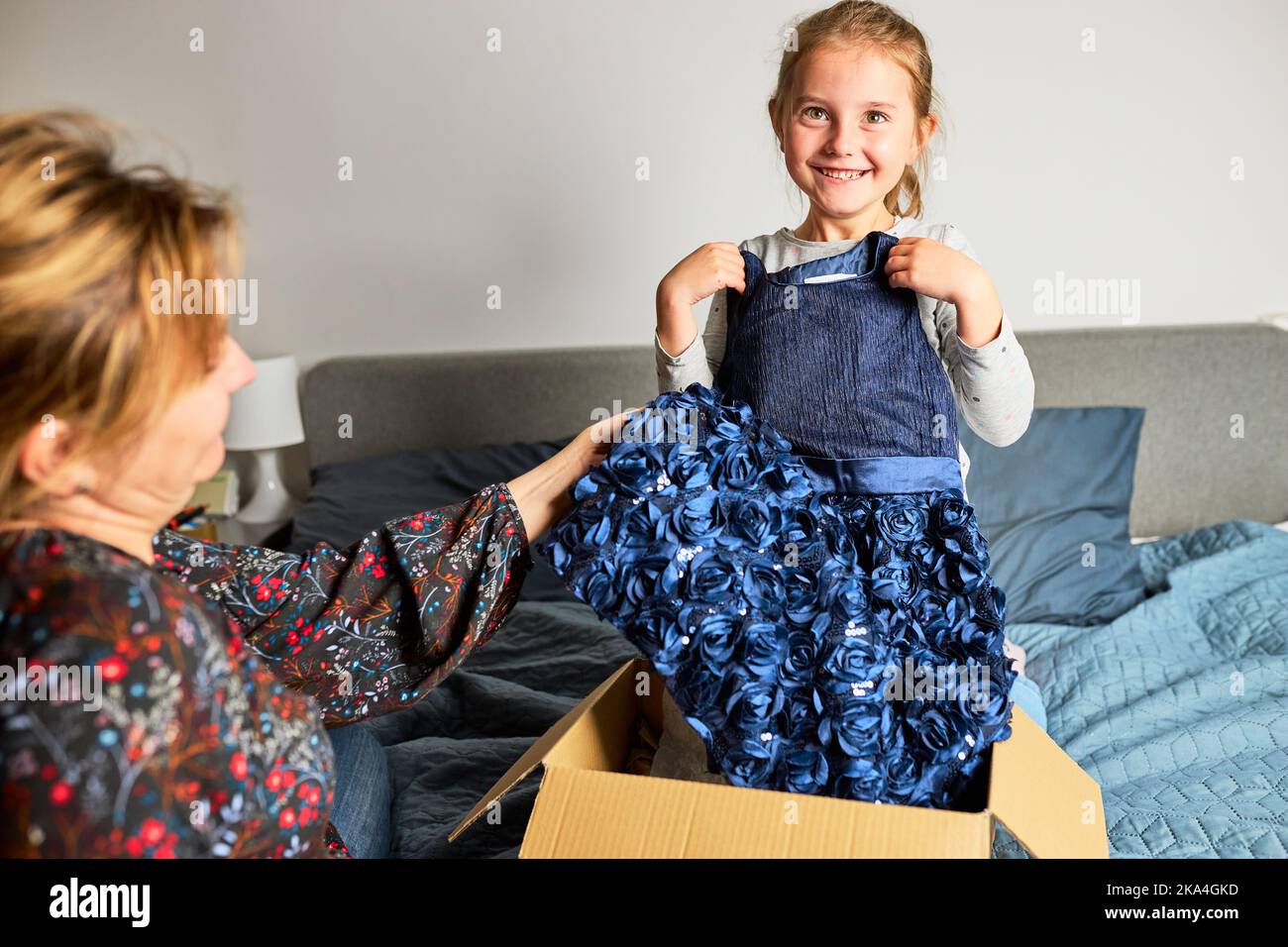 Mother and her daughter opening box with ordered dress at home on couch ...