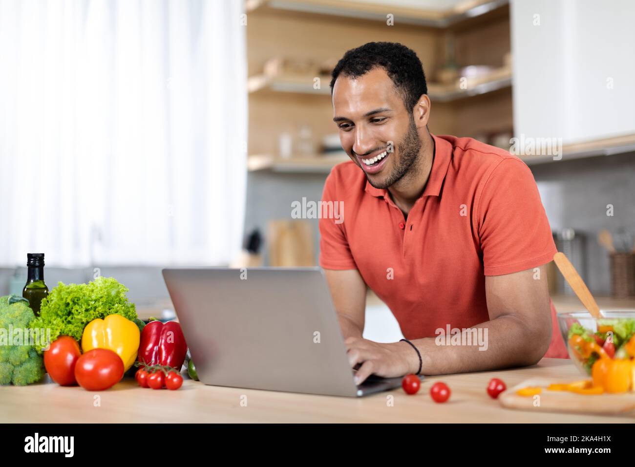 Smiling young black handsome guy in red t-shirt typing on computer ...