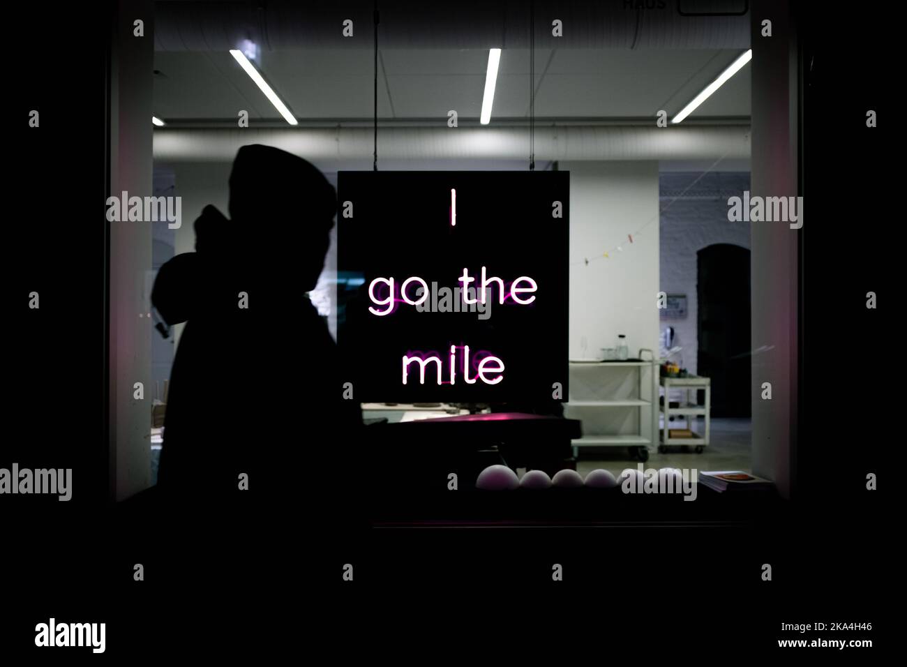 The silhouette of the man passing by the shop window with the neon ...