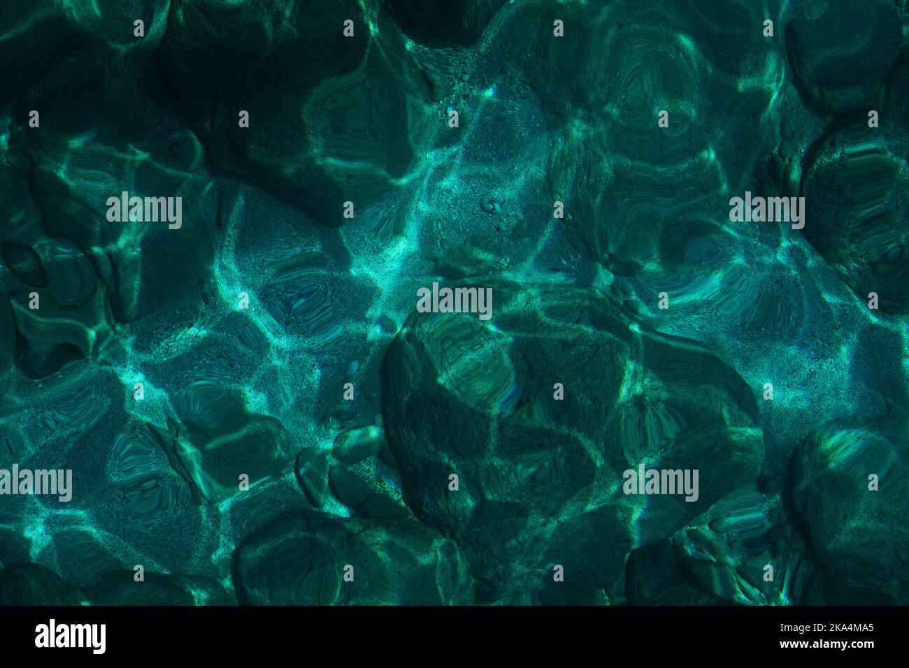 View from above to a stony seabed in clear water with abstract blue ...