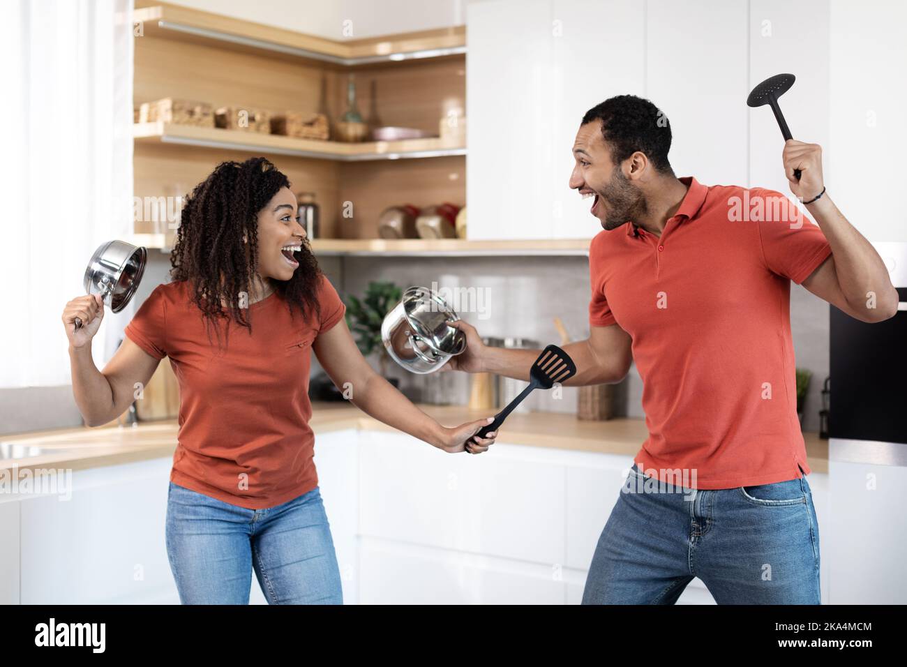 Cheerful young black husband and wife in red t-shirts with utensils ...