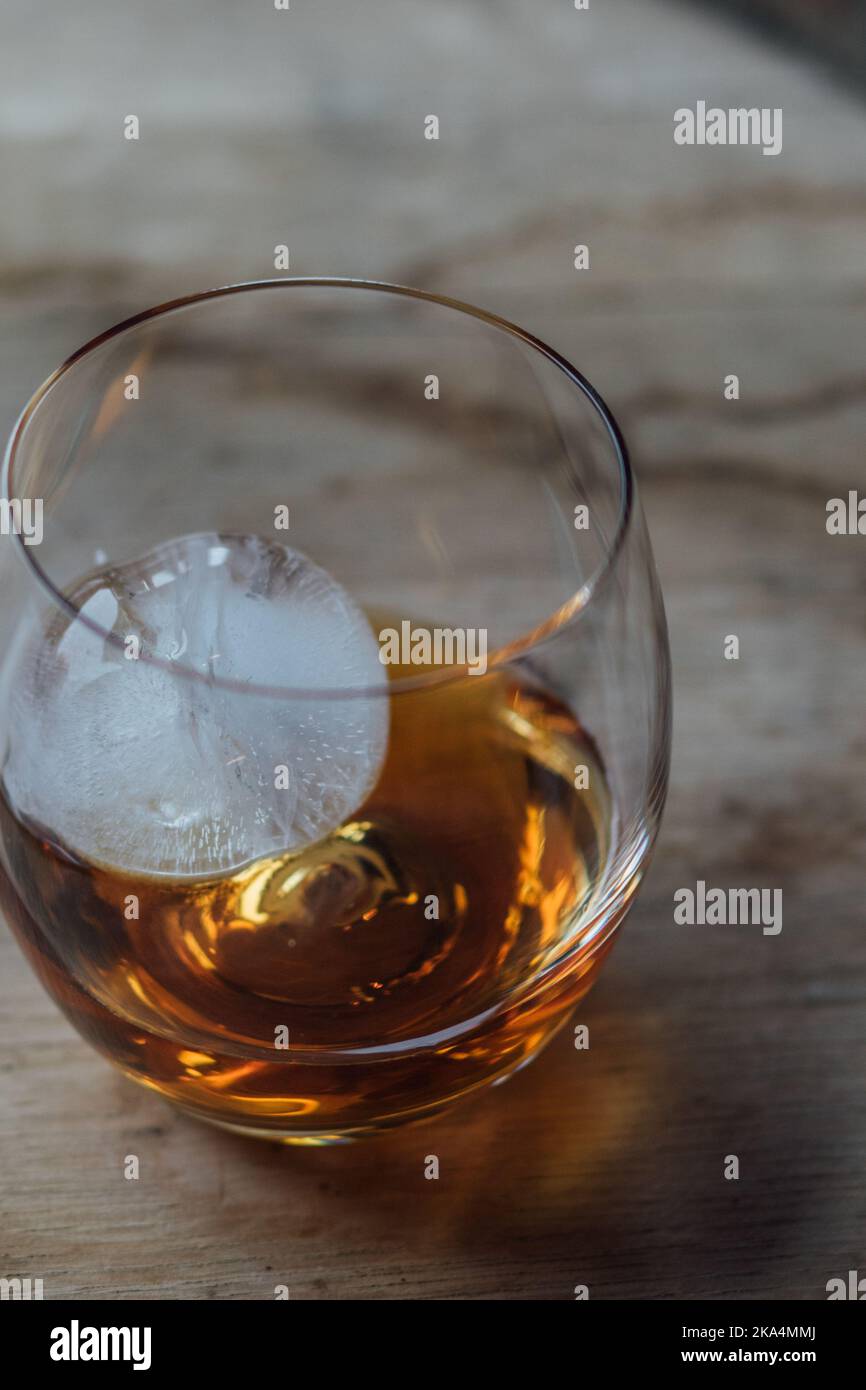 glass dram of whiskey whisky with sphere ice on wood table, barrel ...