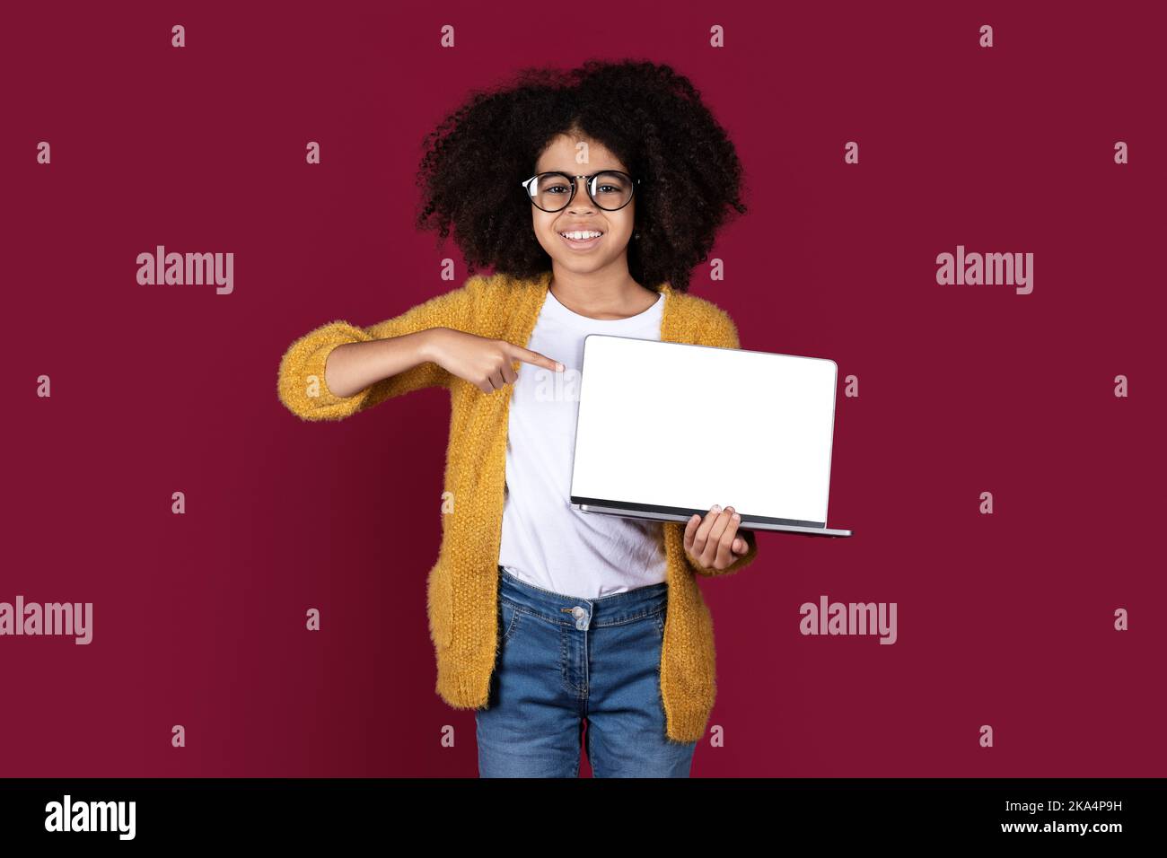 Cute african american schooler showing computer with blank screen ...