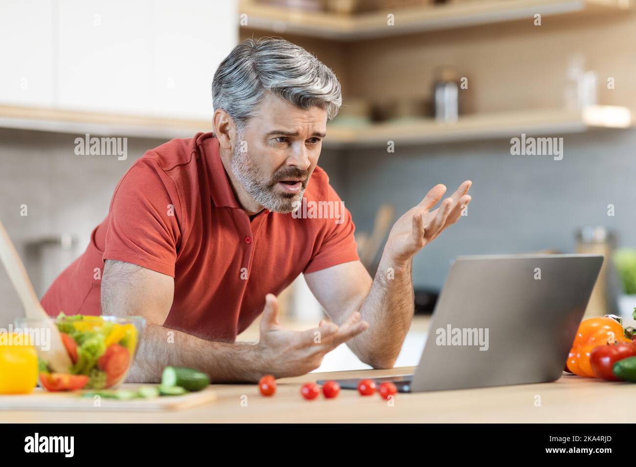 Angry middle aged man looking at computer screen while cooking Stock ...