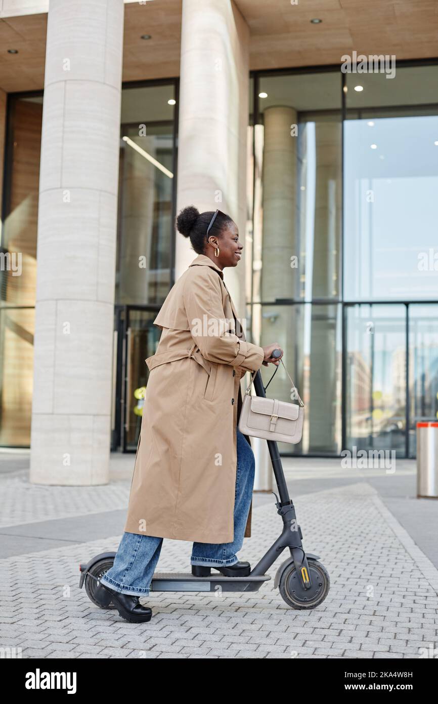 Vertical side view portrait of young black woman riding electric ...