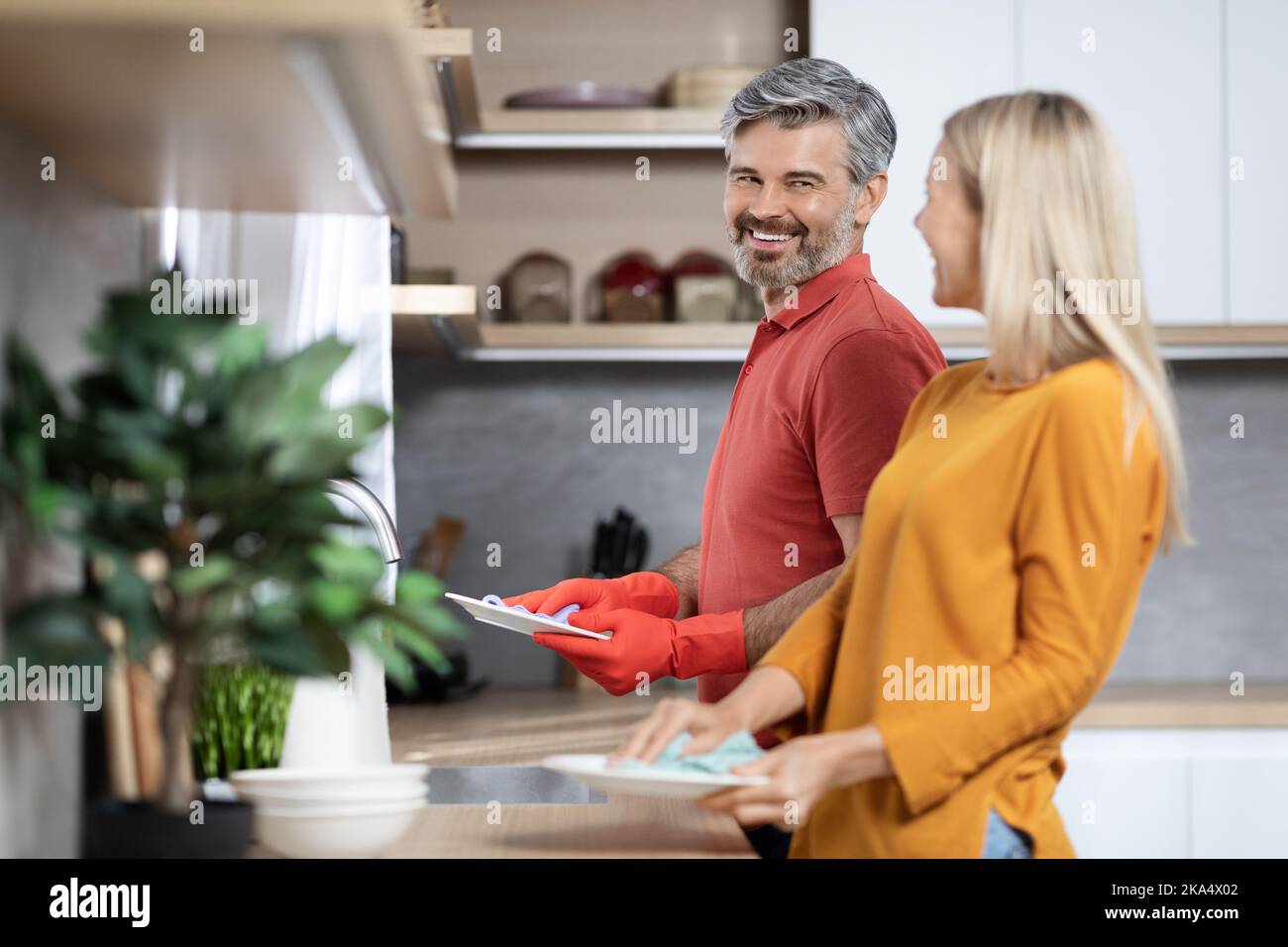 Handsome middle aged husband helping wife with chores, washing dishes ...