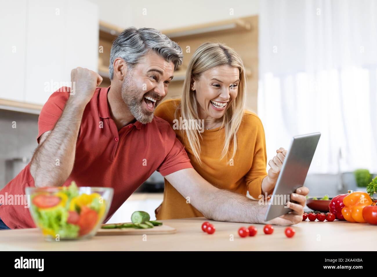 Emotional spouses using digital tablet while cooking, celebrating ...
