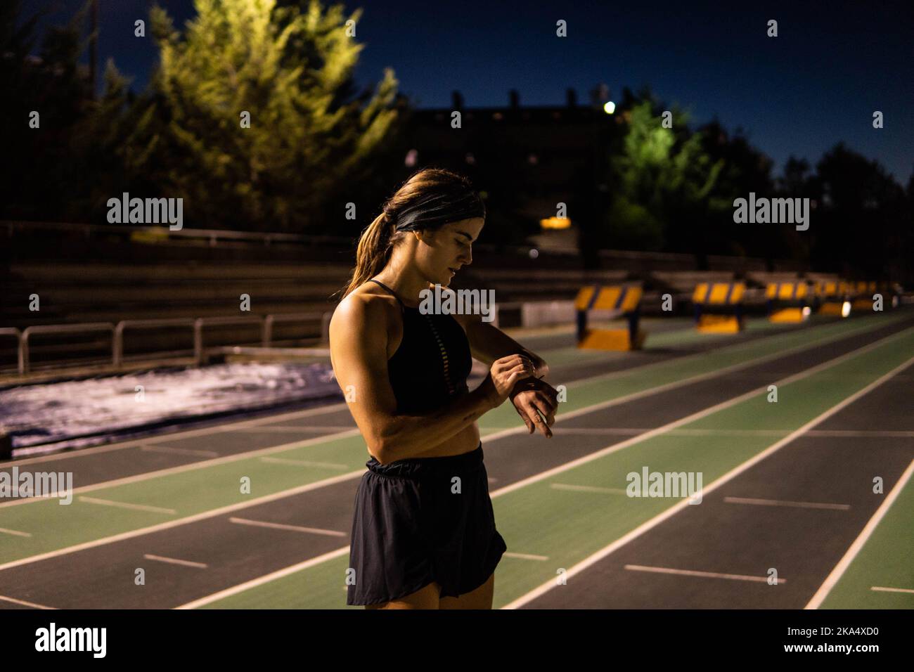woman looking at the watch on a running track at night Stock Photo - Alamy