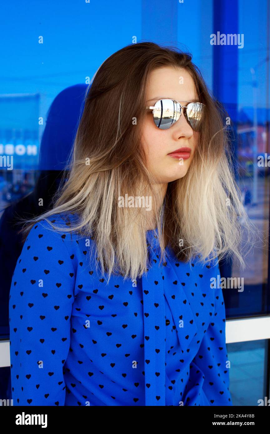 A teenage girl stands in front of the blue windows of a supermarket ...