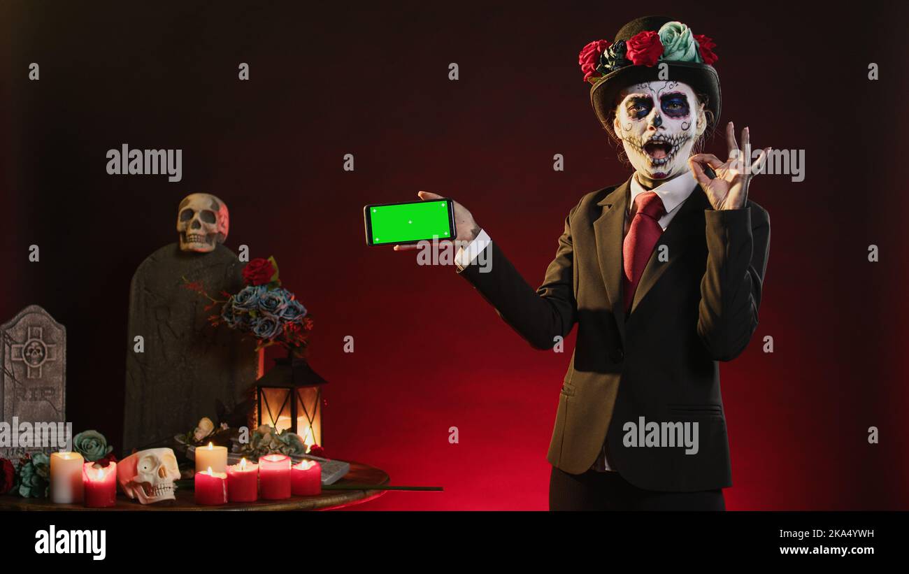 Santa muerte holding horizontal greenscreen on mobile phone, looking at ...