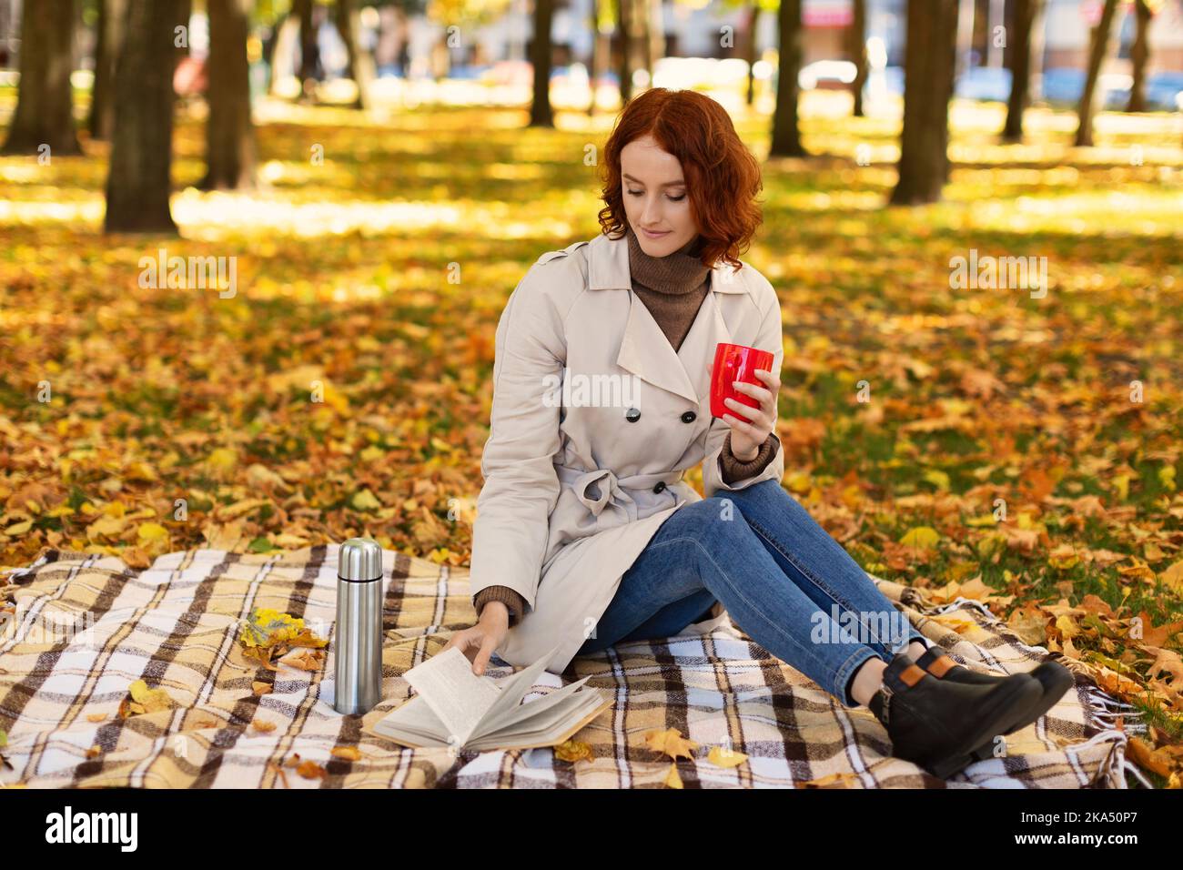 Serious smart young european red-haired lady in raincoat enjoy cup of ...