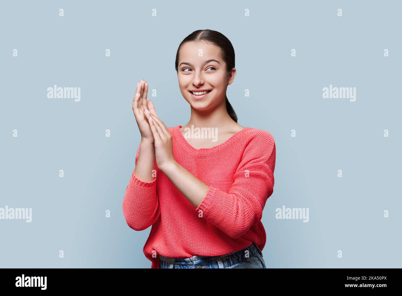 Young teenage girl clapping her hands on grey color studio background ...