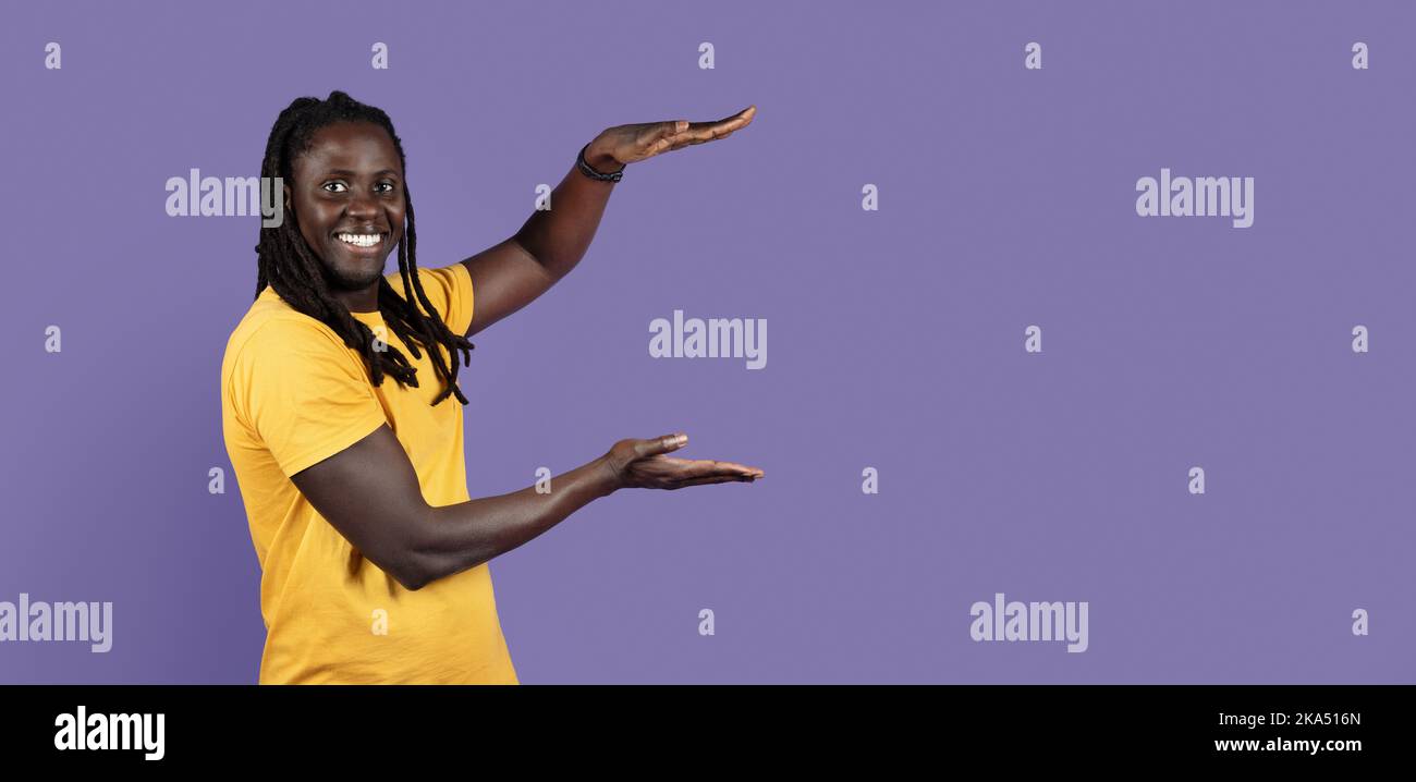 Cheerful african american guy holding something invisible in his hands ...