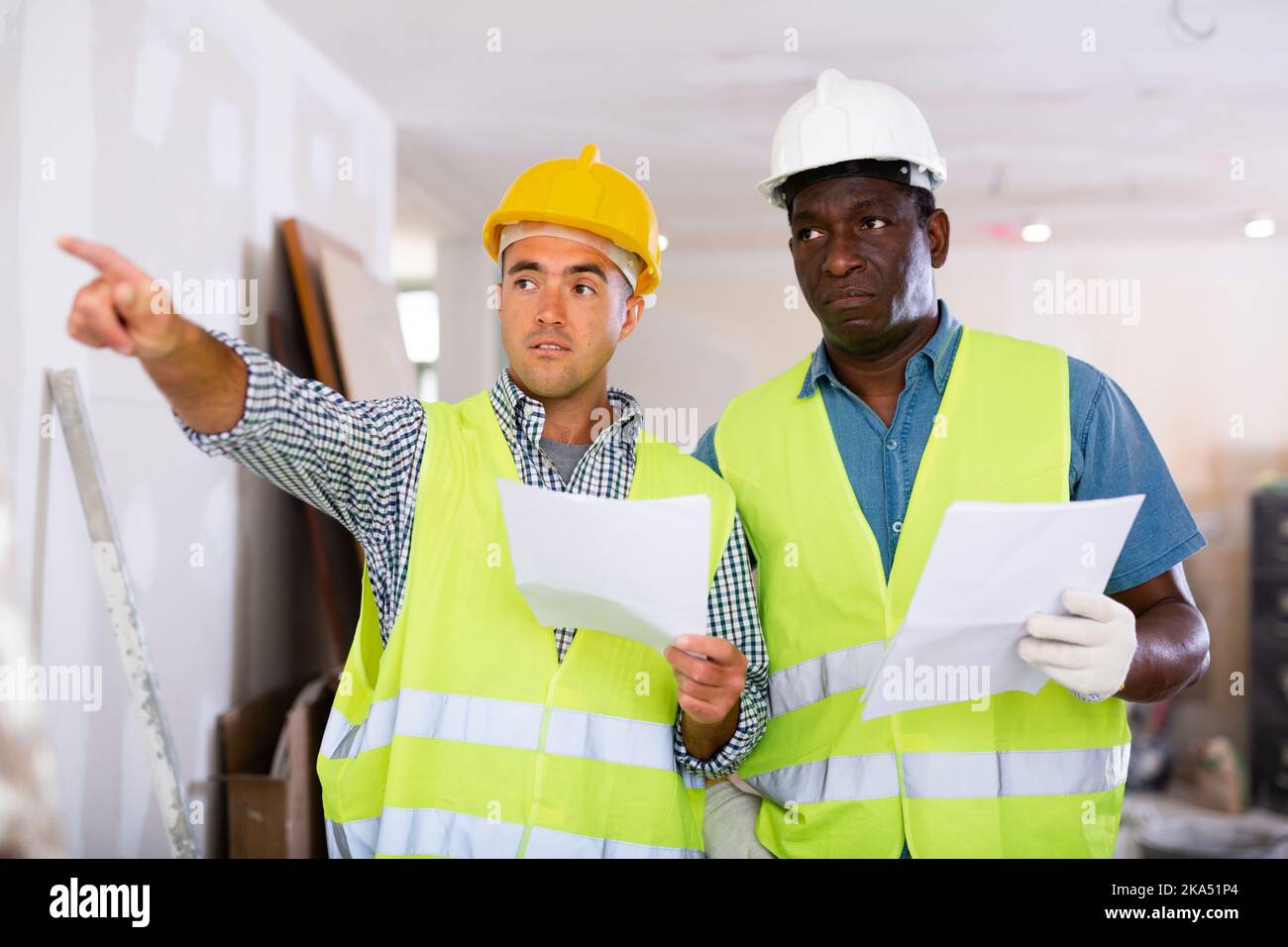 Foreman and worker in yellow vest and protective helmet are discussing ...