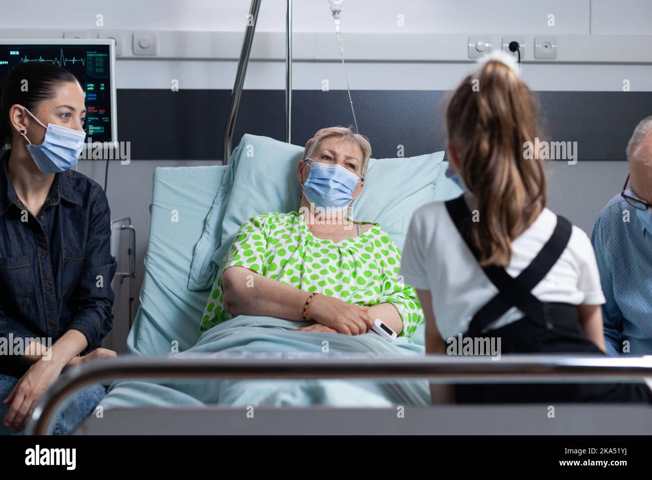 Older female adult resting in hospital bed with family after medical ...