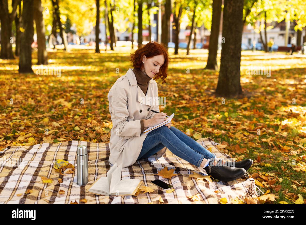 Concentrated smart young european red-haired lady student in raincoat ...