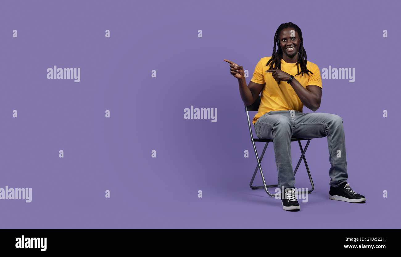 Relaxed black man sitting on chair, pointing at copy space Stock Photo ...