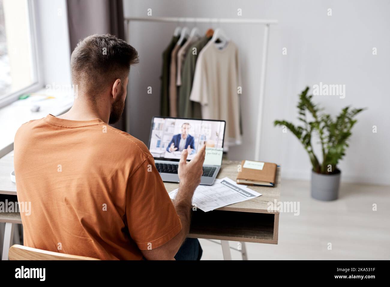Back view of young man sitting in front of laptop with tutor on screen ...