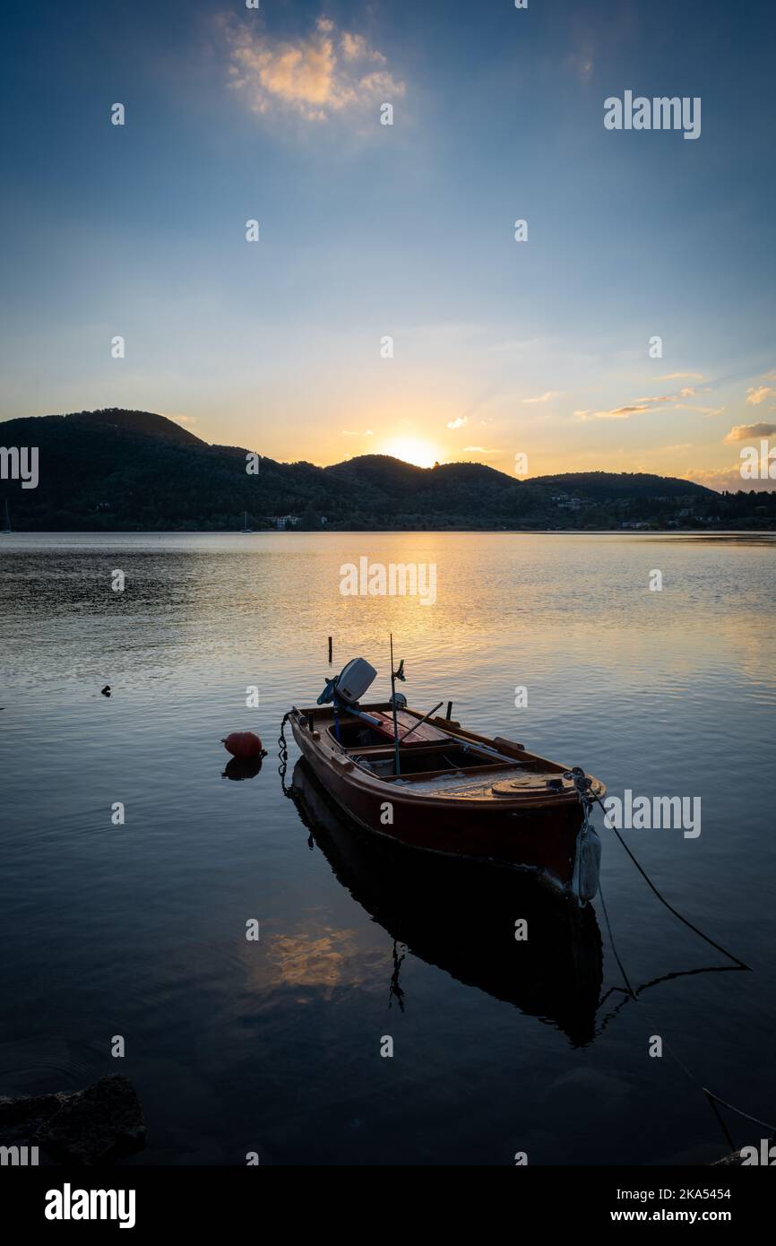 A old wooden boat on a sea bay with calm waters with the sun rising ...