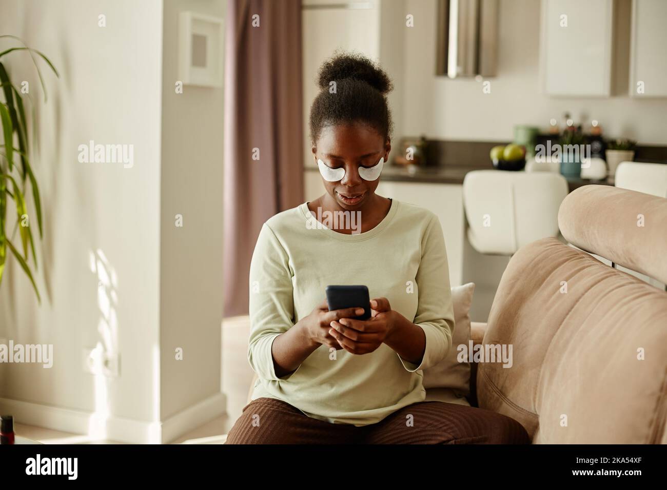 Close up of black young woman wearing eye mask and using smartphone ...