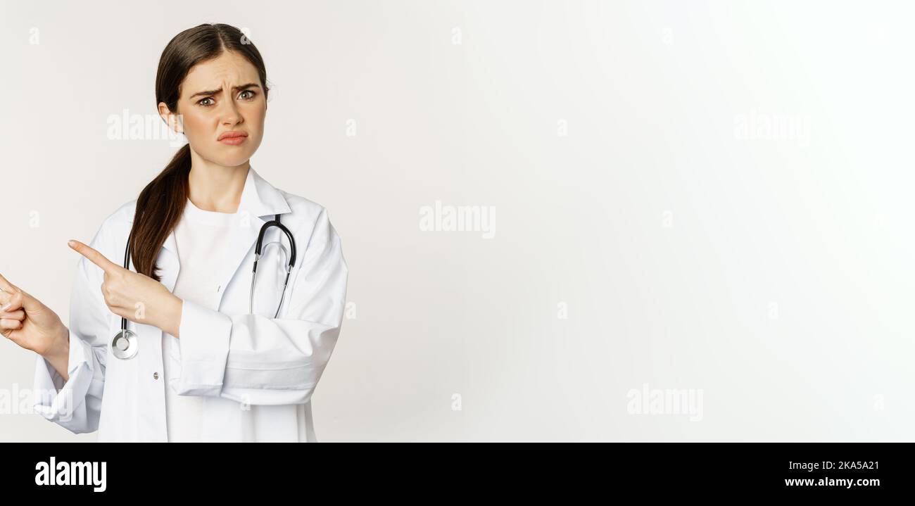 Sad and disappointed female doctor, frowning frustrated, pointing ...