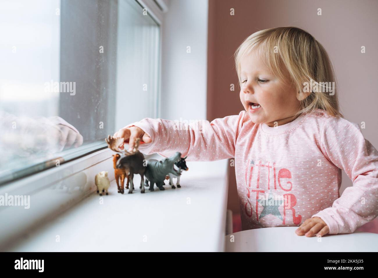 Little girl toddler playing with animal toys on window sill in children ...