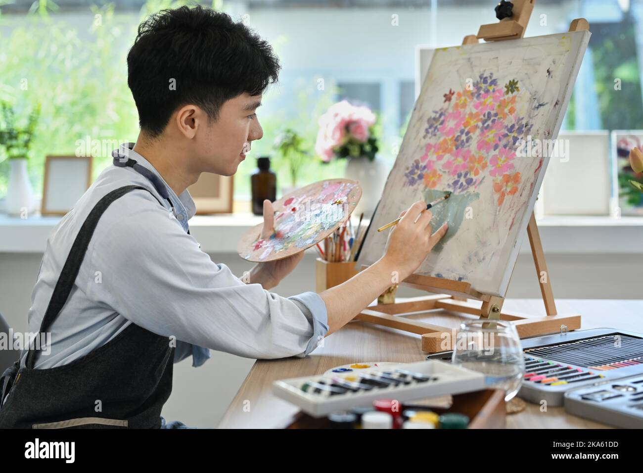 Side view of asian man painting with watercolor on canvas in bright ...