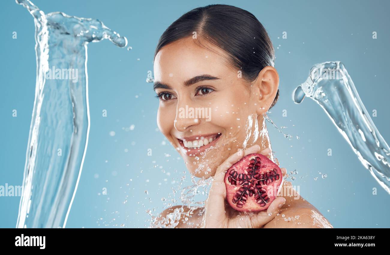 Woman, beauty and water splash with pomegranate, skincare and happy against a blue studio ...
