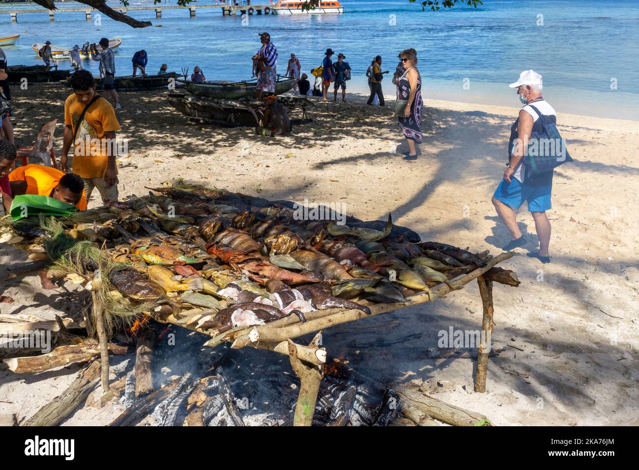 Locals preparing and cooking fish on open fire on beach, Kiriwina ...