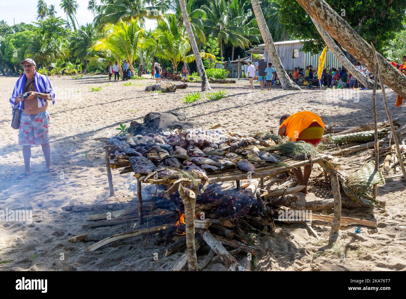 Locals preparing and cooking fish on open fire on beach, Kiriwina ...