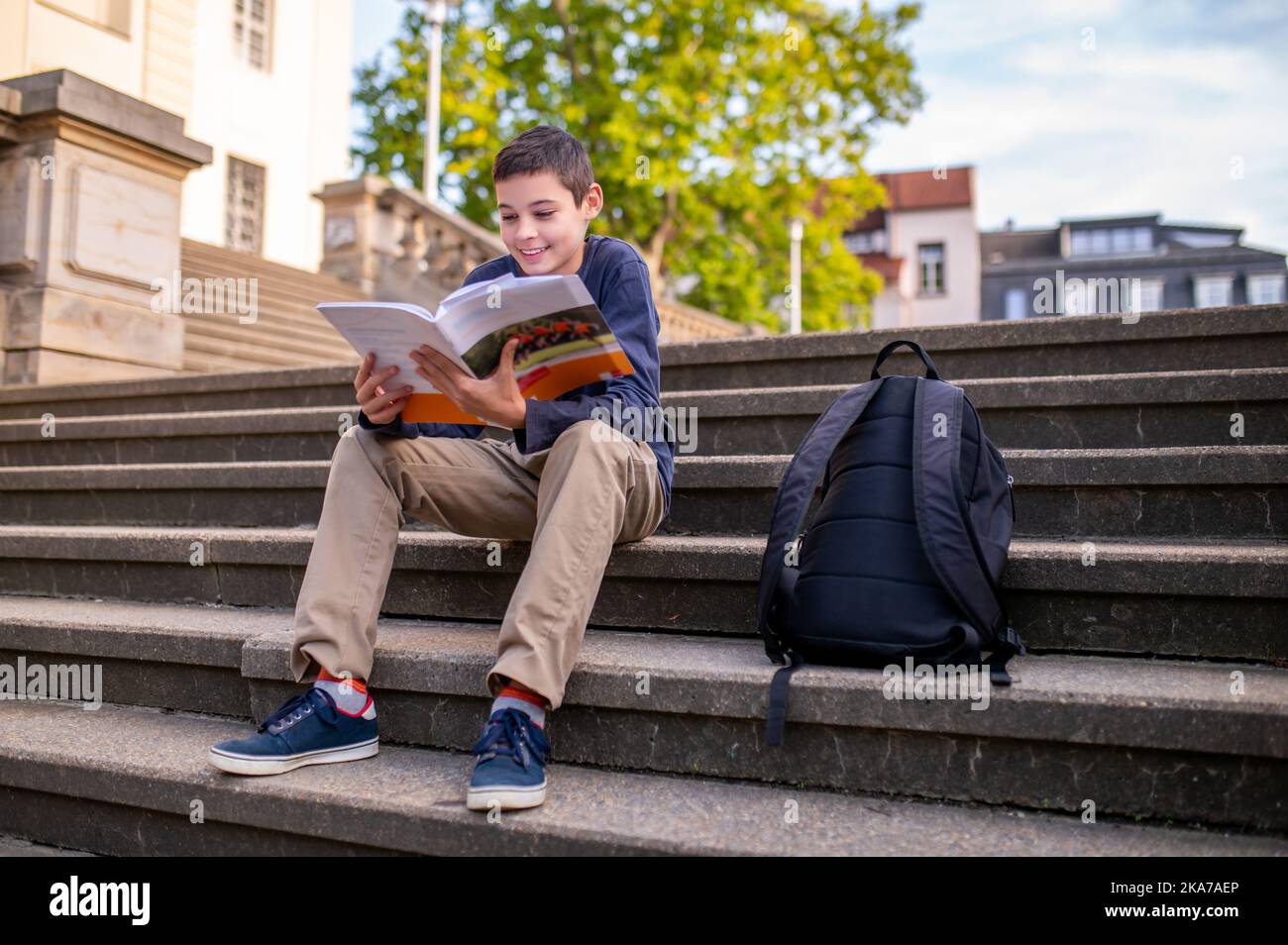 Cute teen reading a book seated on the stairs Stock Photo - Alamy