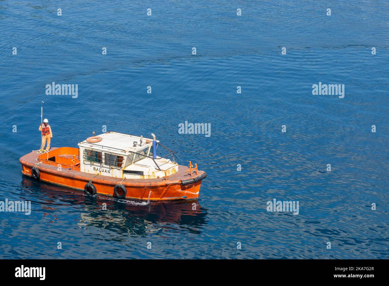 Man standing on back of orange port tender ready to receive mooring ...