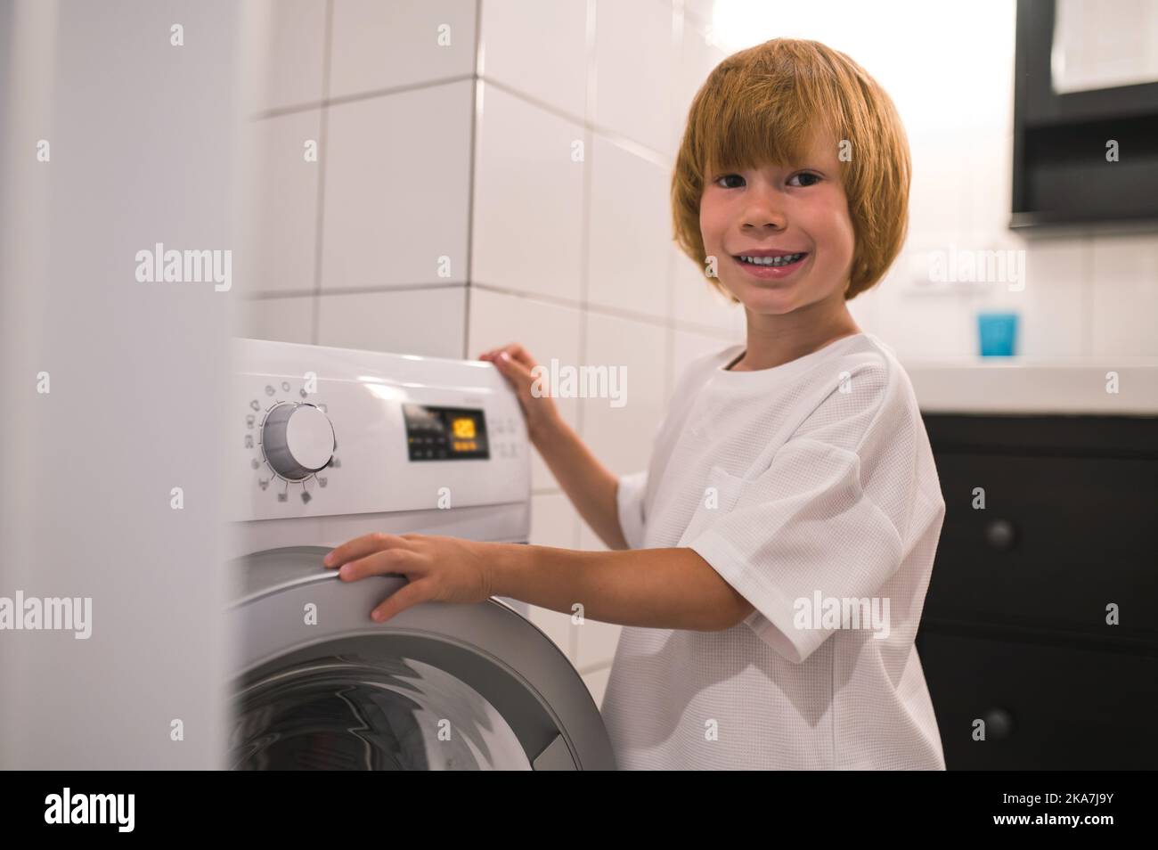 Little ginger boy switching on a washing machine Stock Photo - Alamy
