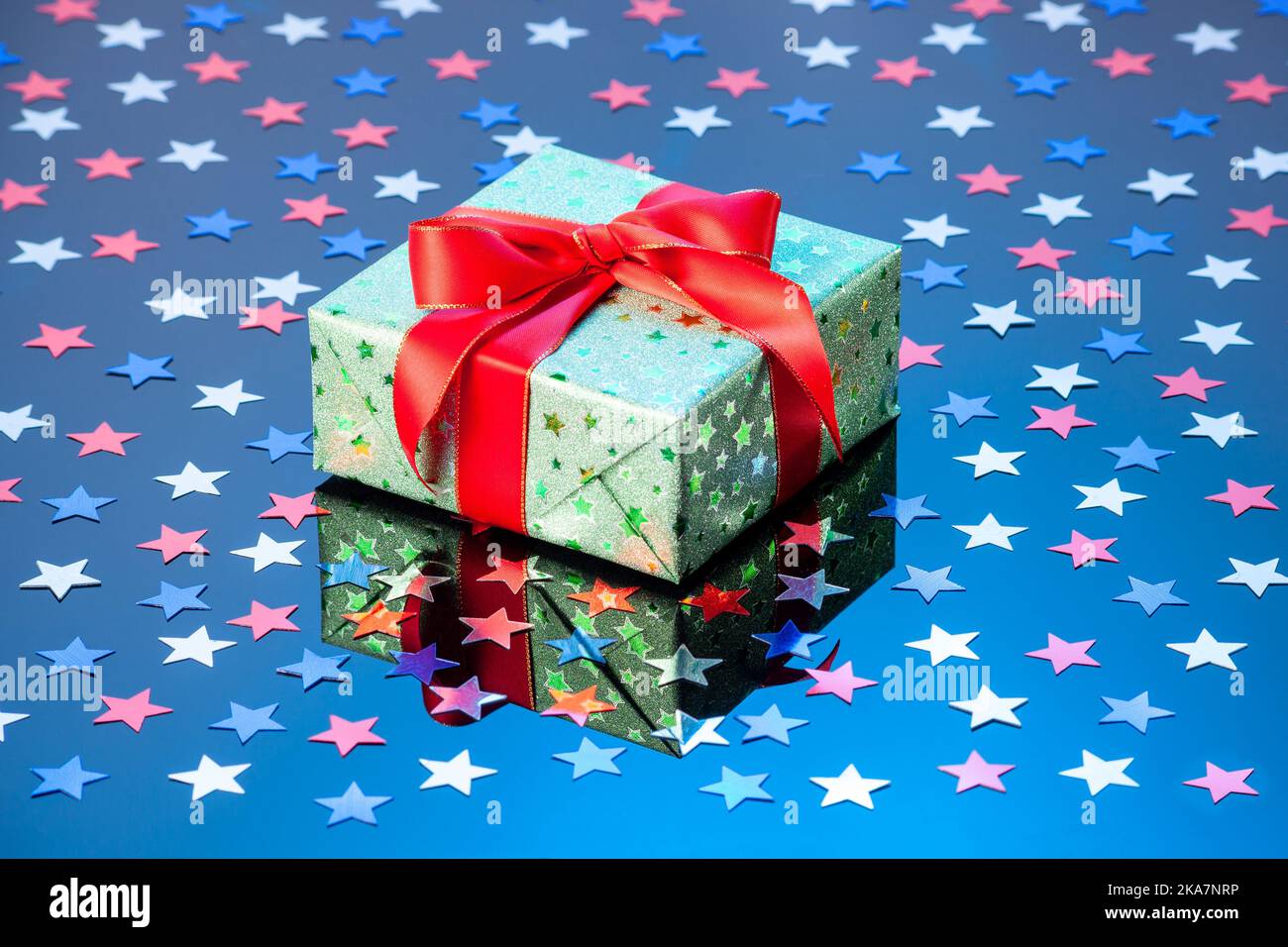 Single green gift box with red ribbon bow on blue reflective surface ...