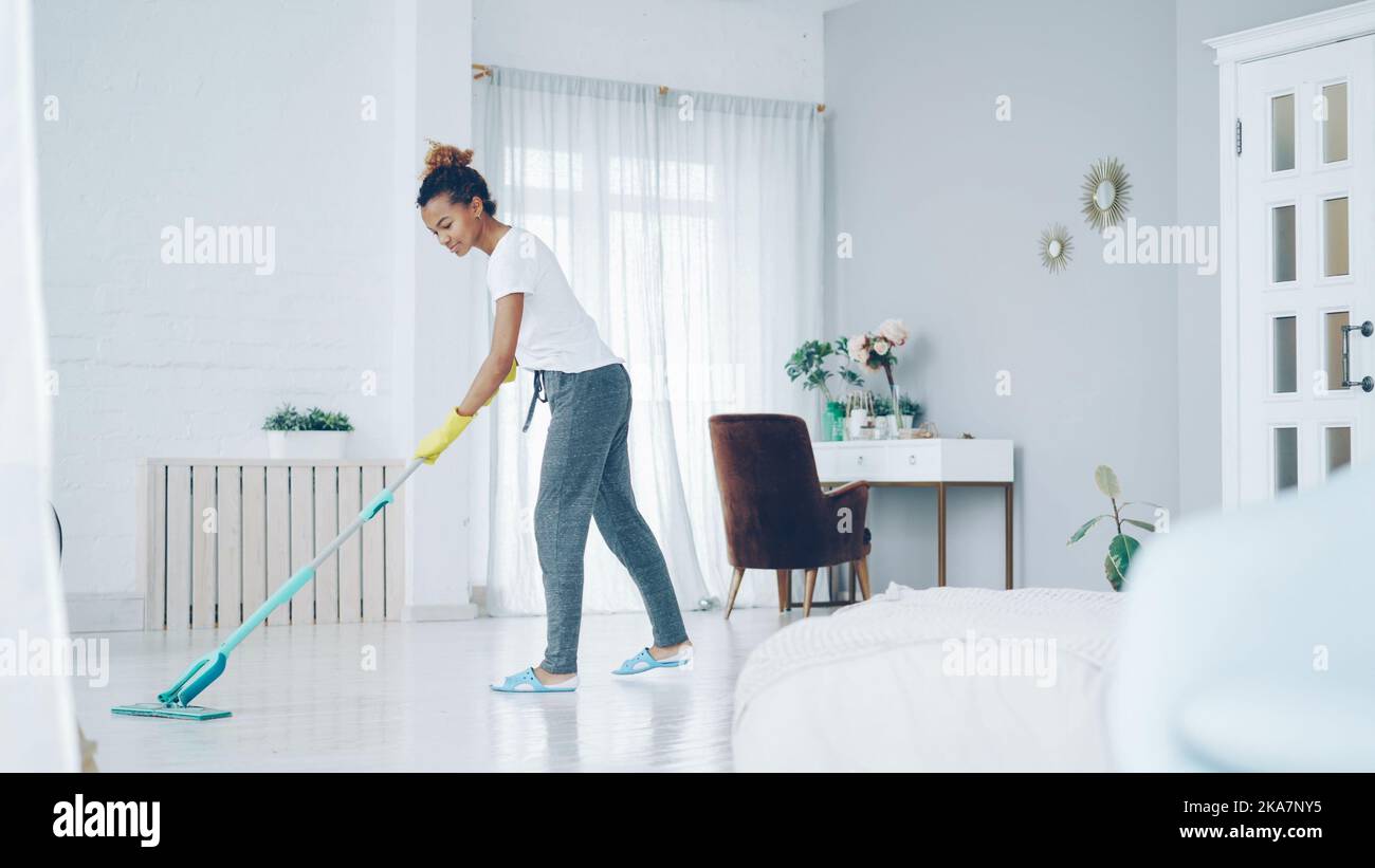 Pretty African American girl is mopping floor at home with flat plastic ...