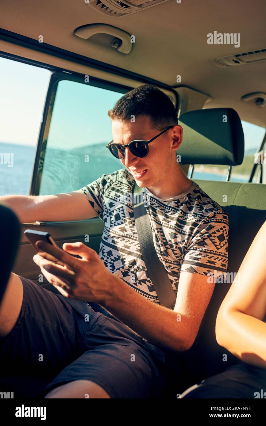 On route to the beach. a young man using a cellphone in a car on a road ...